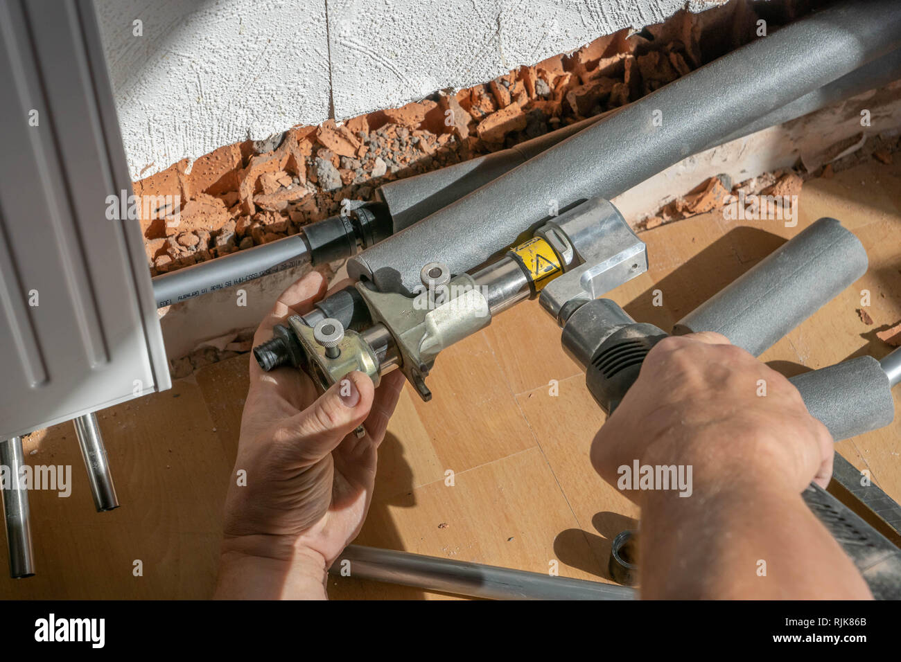 Installer squeezes plastic pipes for the radiator Stock Photo - Alamy