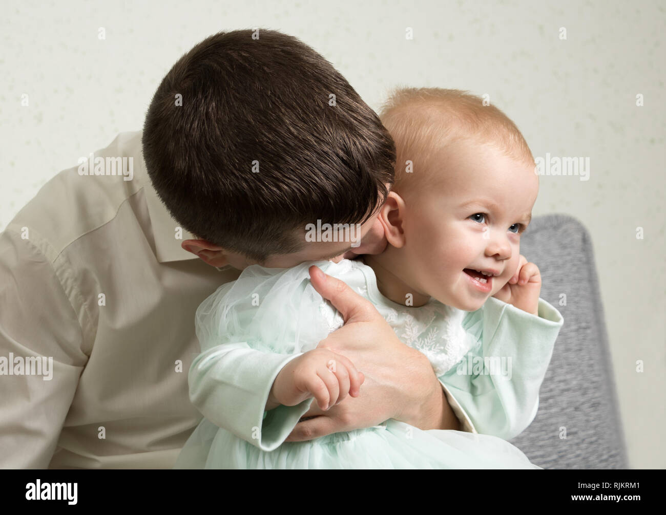 father plays with her little daughter, tickles her neck with kisses ...