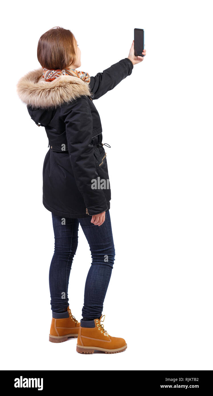 Back view woman in winter jacket who makes selfie with a smartphone ...