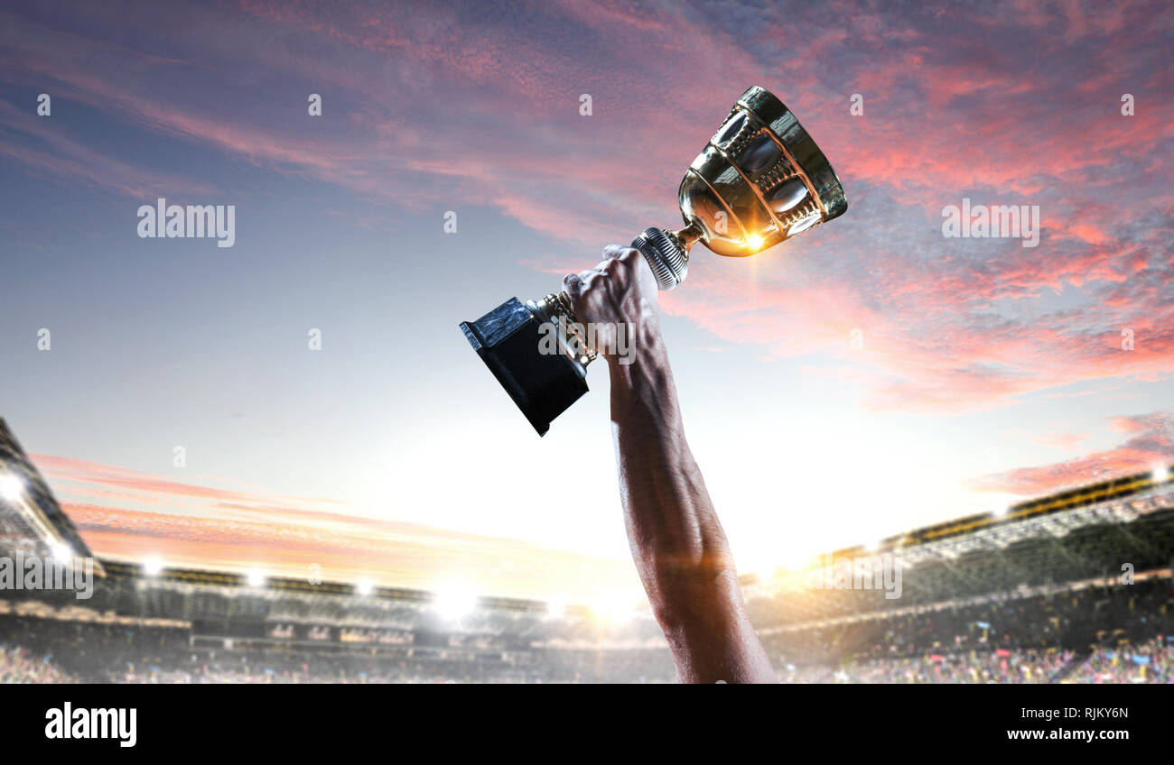 Hand of athlete holding cup trophy against stadium. Mixed media Stock ...