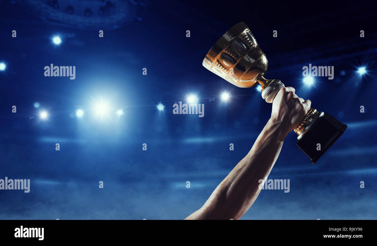 Hand of athlete holding cup trophy against stadium. Mixed media Stock ...