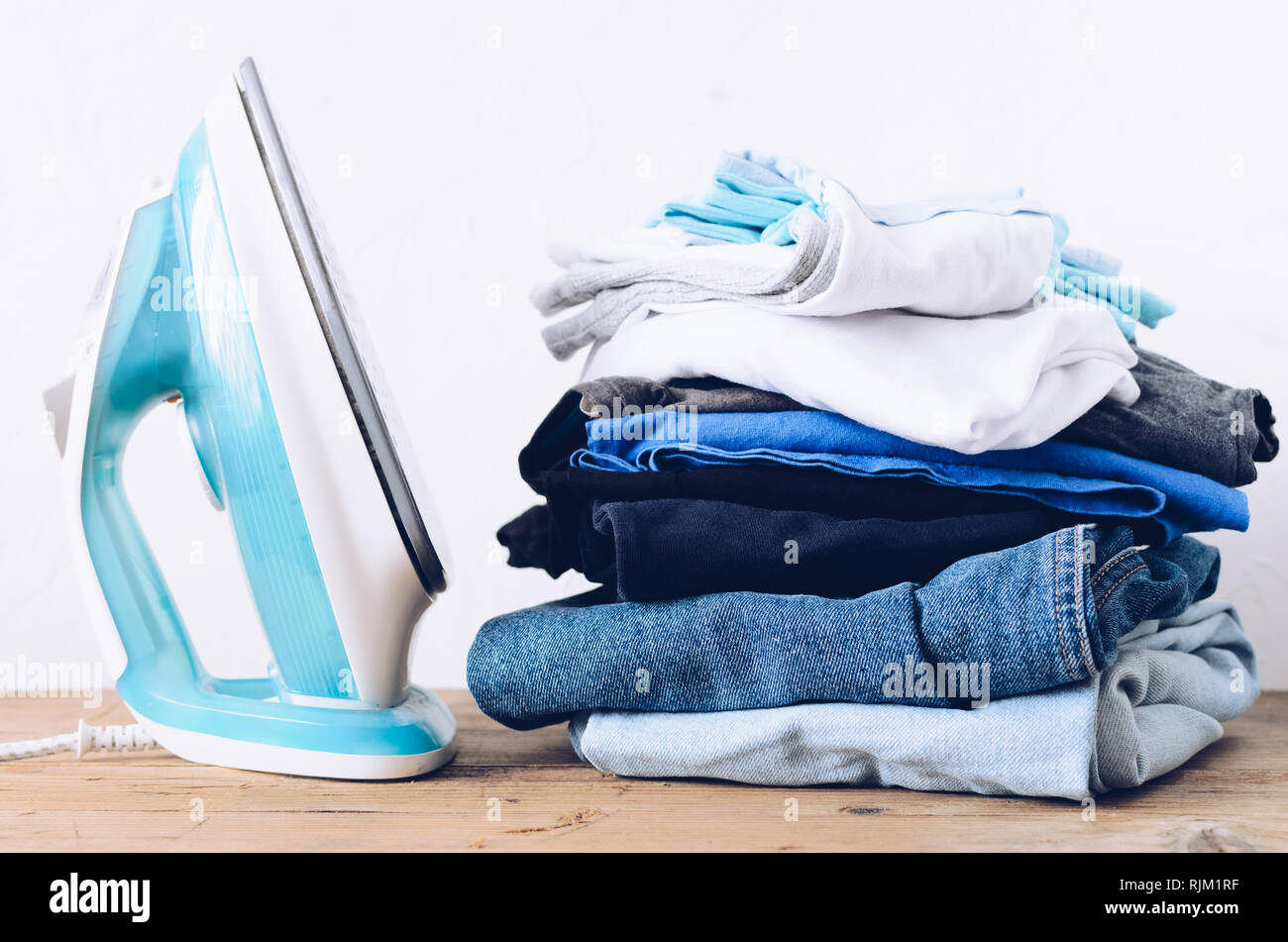 Stack of clothes and electric iron on table indoor. Household concept ...