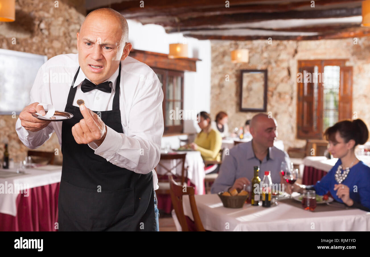 Male waiter expressing his displeasure with small tips from couple of ...