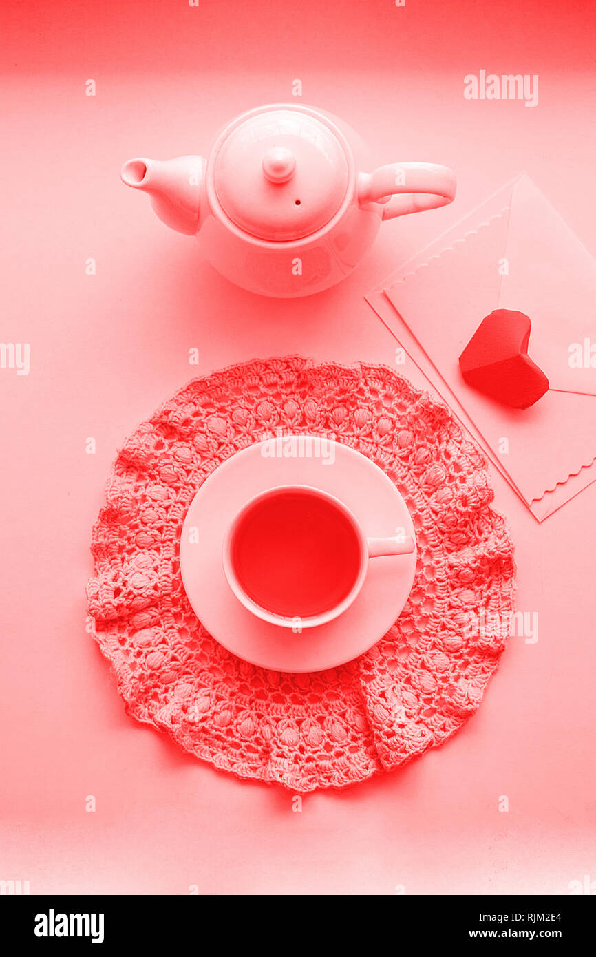 Cup of scented pink tea on crocheting napkin, teapot and envelope on ...