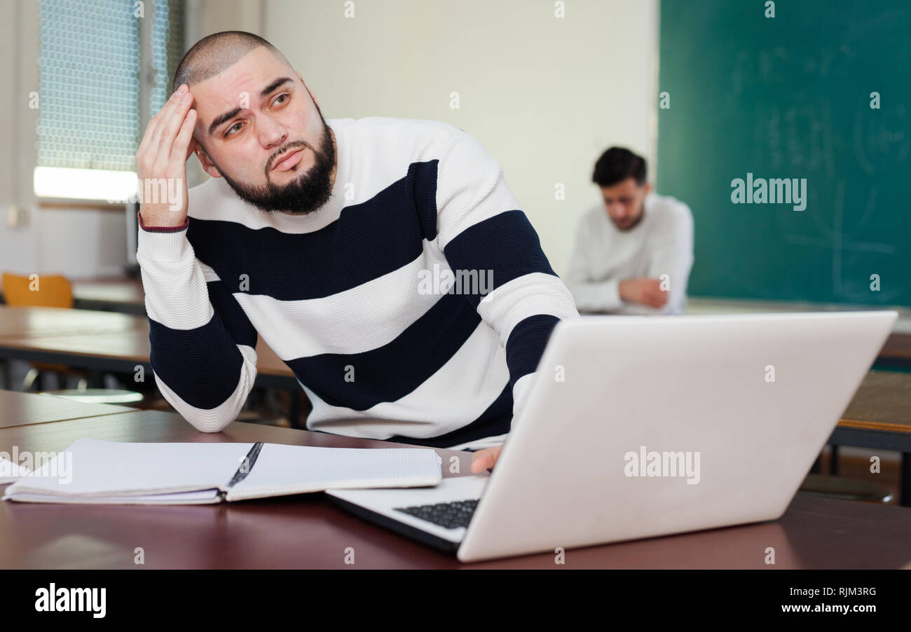 Portrait of male university student sitting at desk and focused on his ...