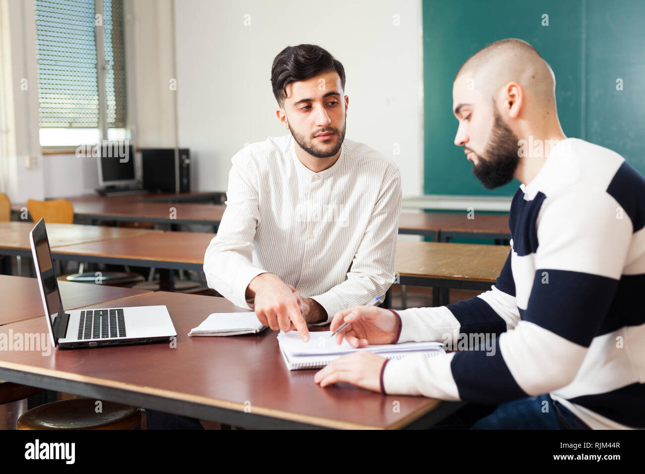 Two young handsome students working with laptop at desk in classroom ...