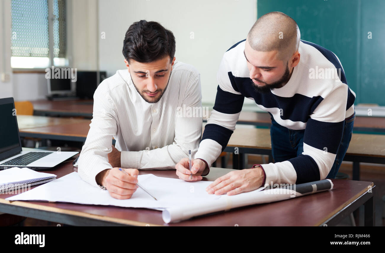Two young handsome students working with laptop at desk in classroom ...