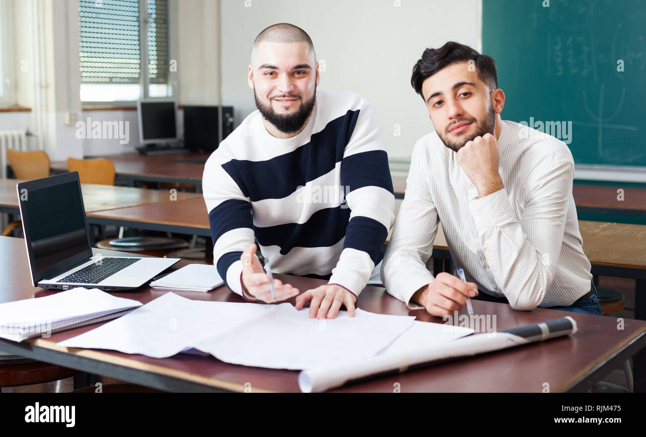 Portrait of two positive male students sitting together at desk in classroom Stock Photo - Alamy