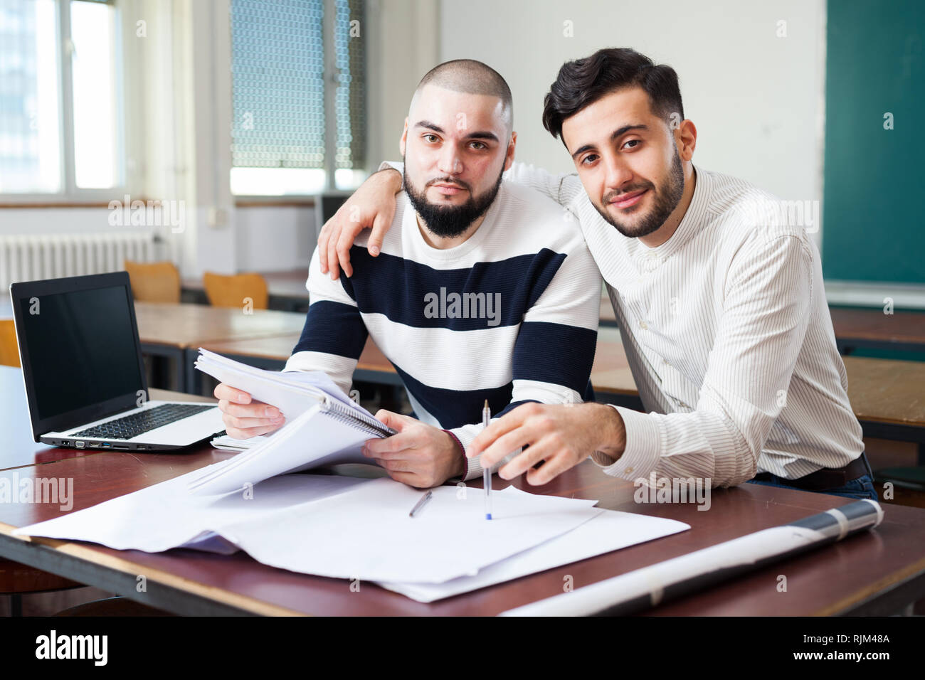 Portrait of two positive male students sitting together at desk in classroom Stock Photo - Alamy