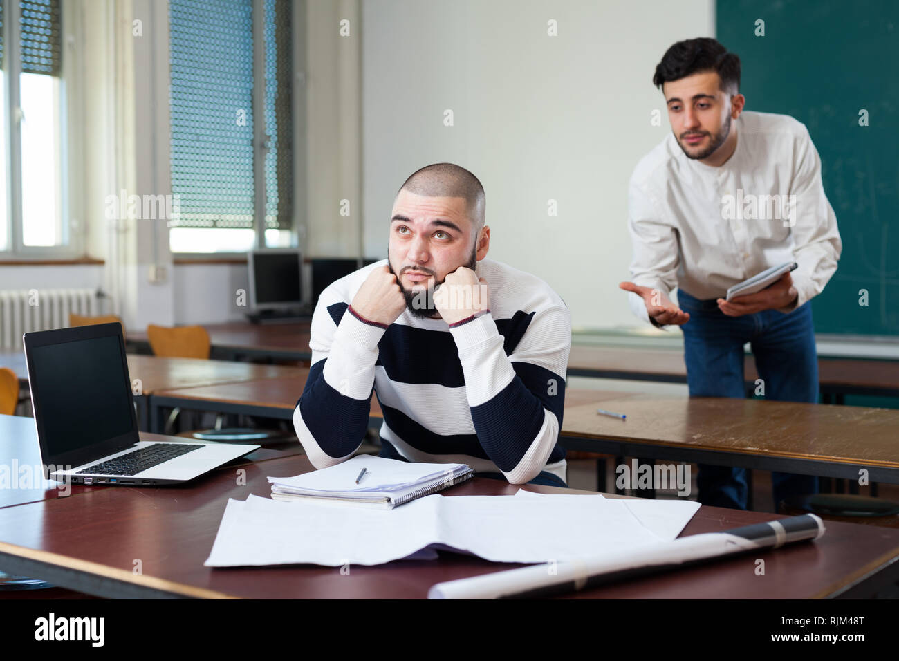 Young man trying to help his worried friend with studies at classroom ...