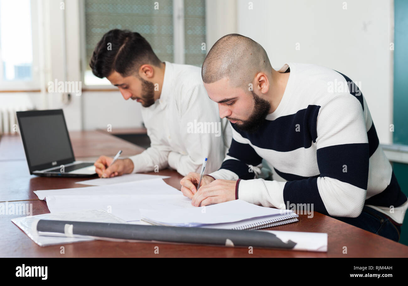 Portrait of two young guys working on their student project at desk in ...