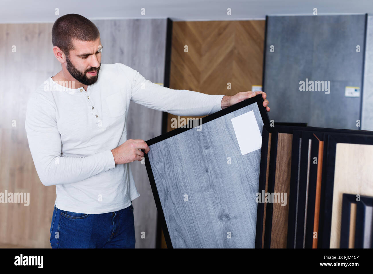 Portrait of young positive man choosing wood laminated flooring in shop ...