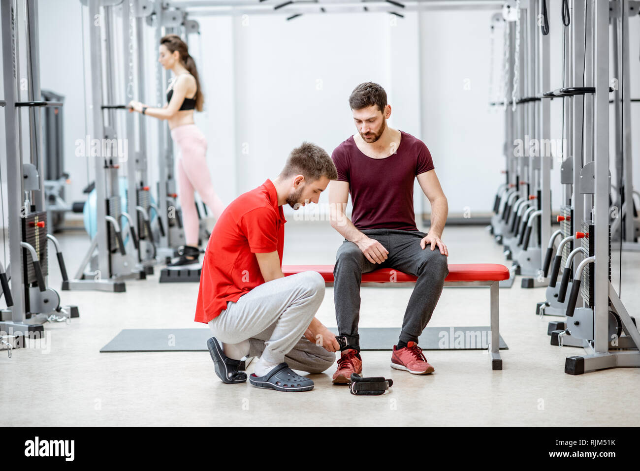 Trainer wearing cuffs on the patient's legs preparing for the exercises ...
