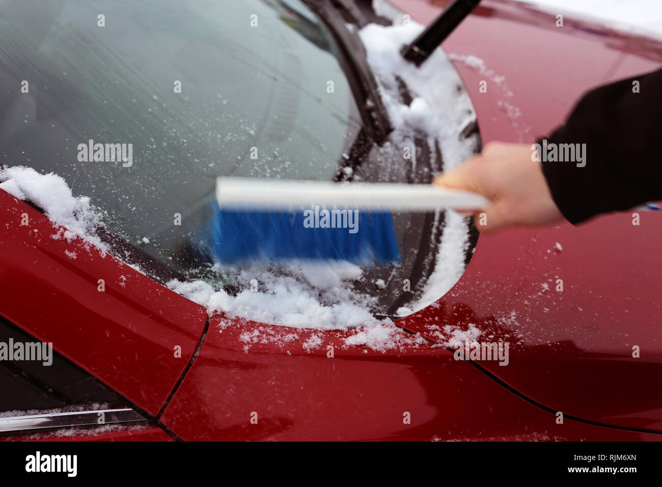 Cleaning the windows of a red car during winter. There is some snow on ...