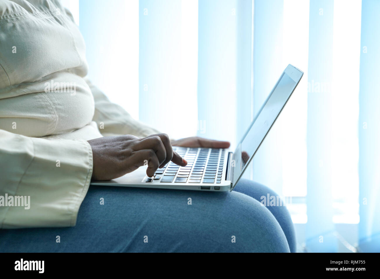 With laptop on her lap and windows at the background, space for text ...