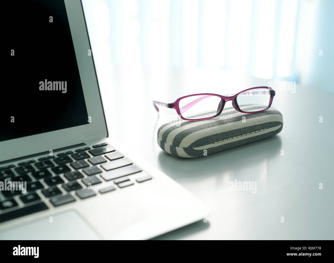 Lap top and spectacles on office desk with windows at the background ...