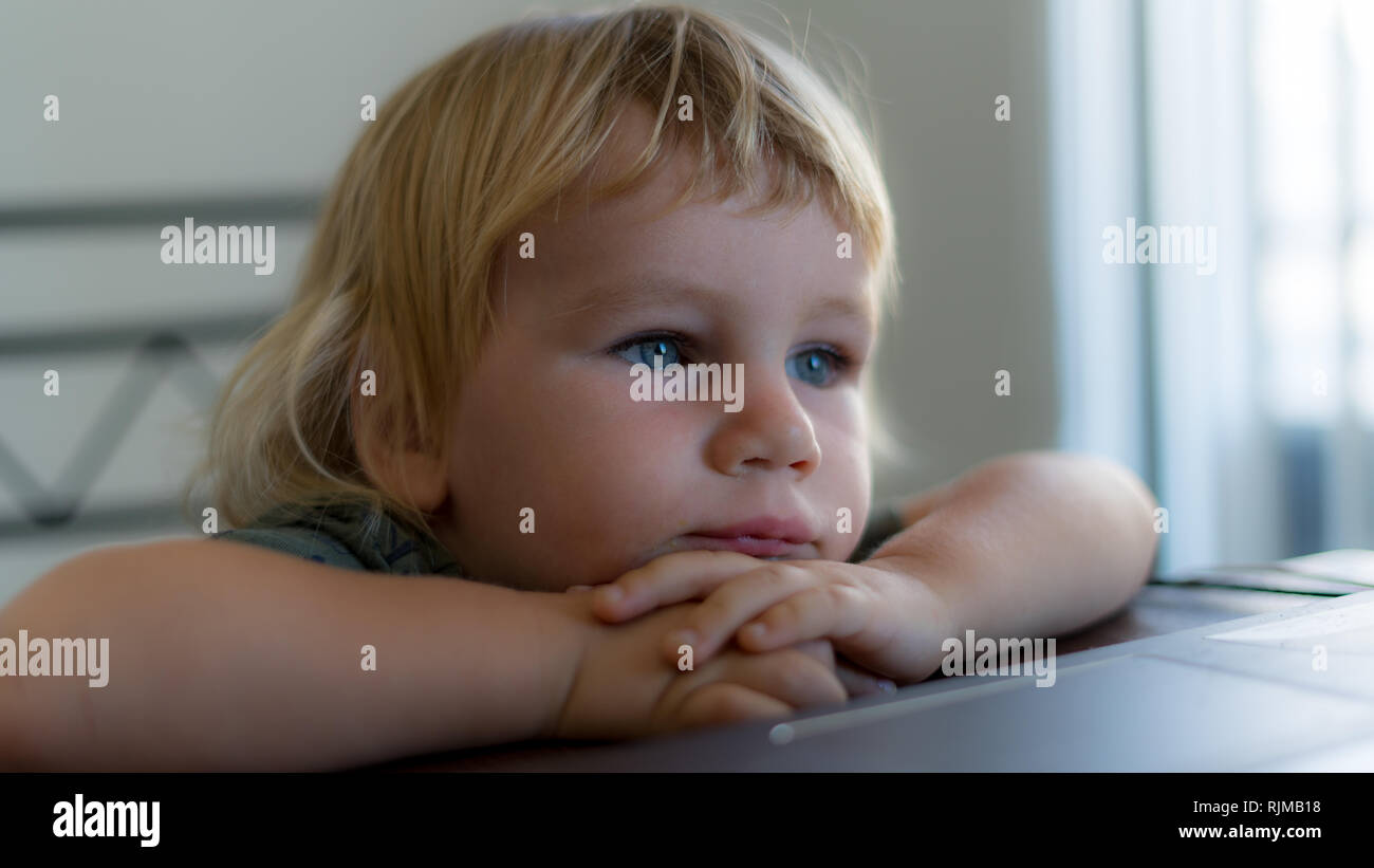 A nice photo of a adorable boy leaning on his hands on a table and ...