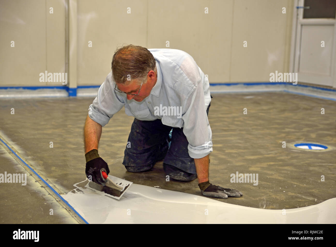 tradesman applying epoxy product to floor of an industrial building ...