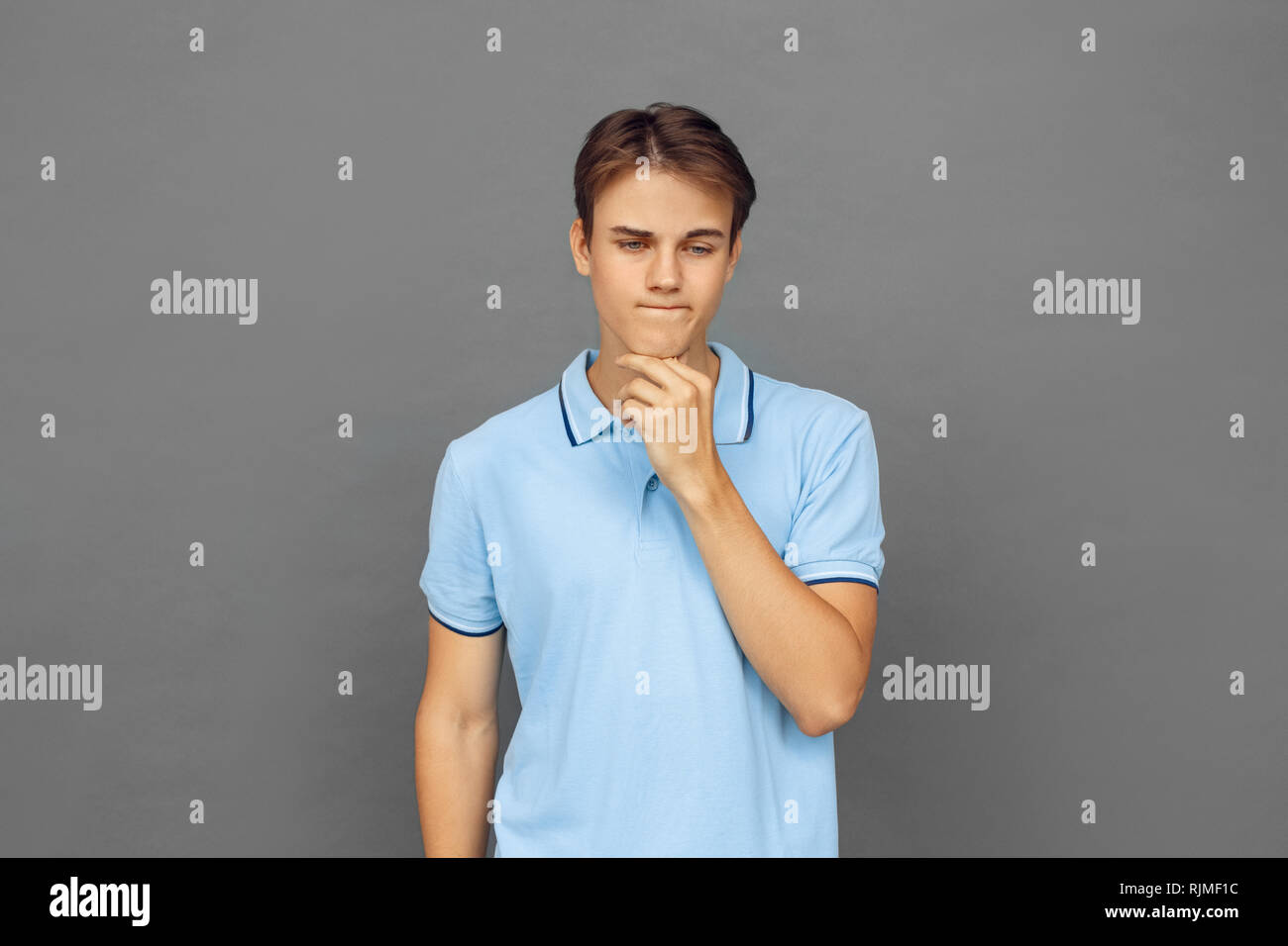 Freestyle. Teenager boy standing isolated on grey touching chin ...