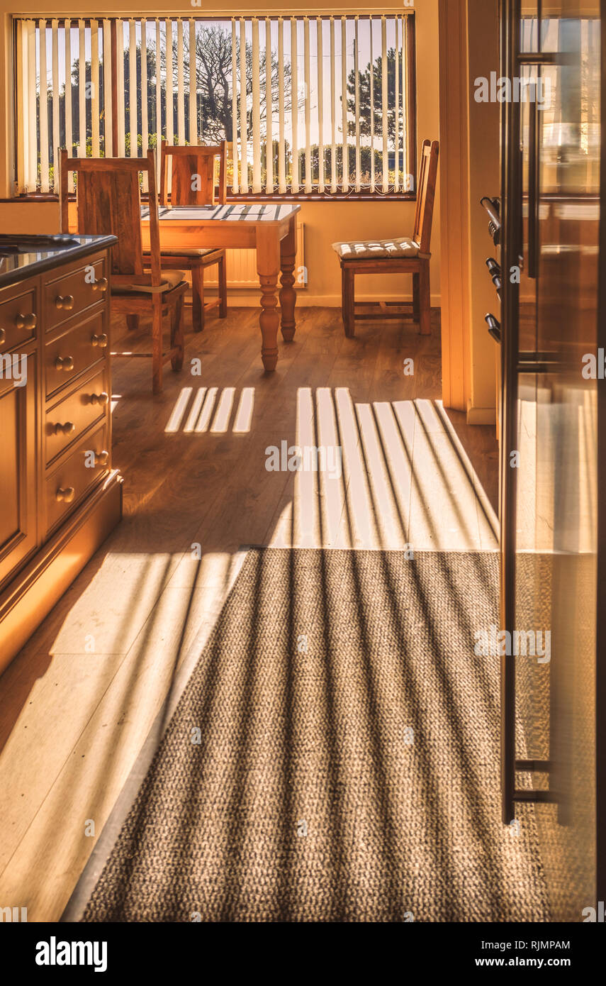 sunlight shining into a kitchen through vertical blinds casting a long ...