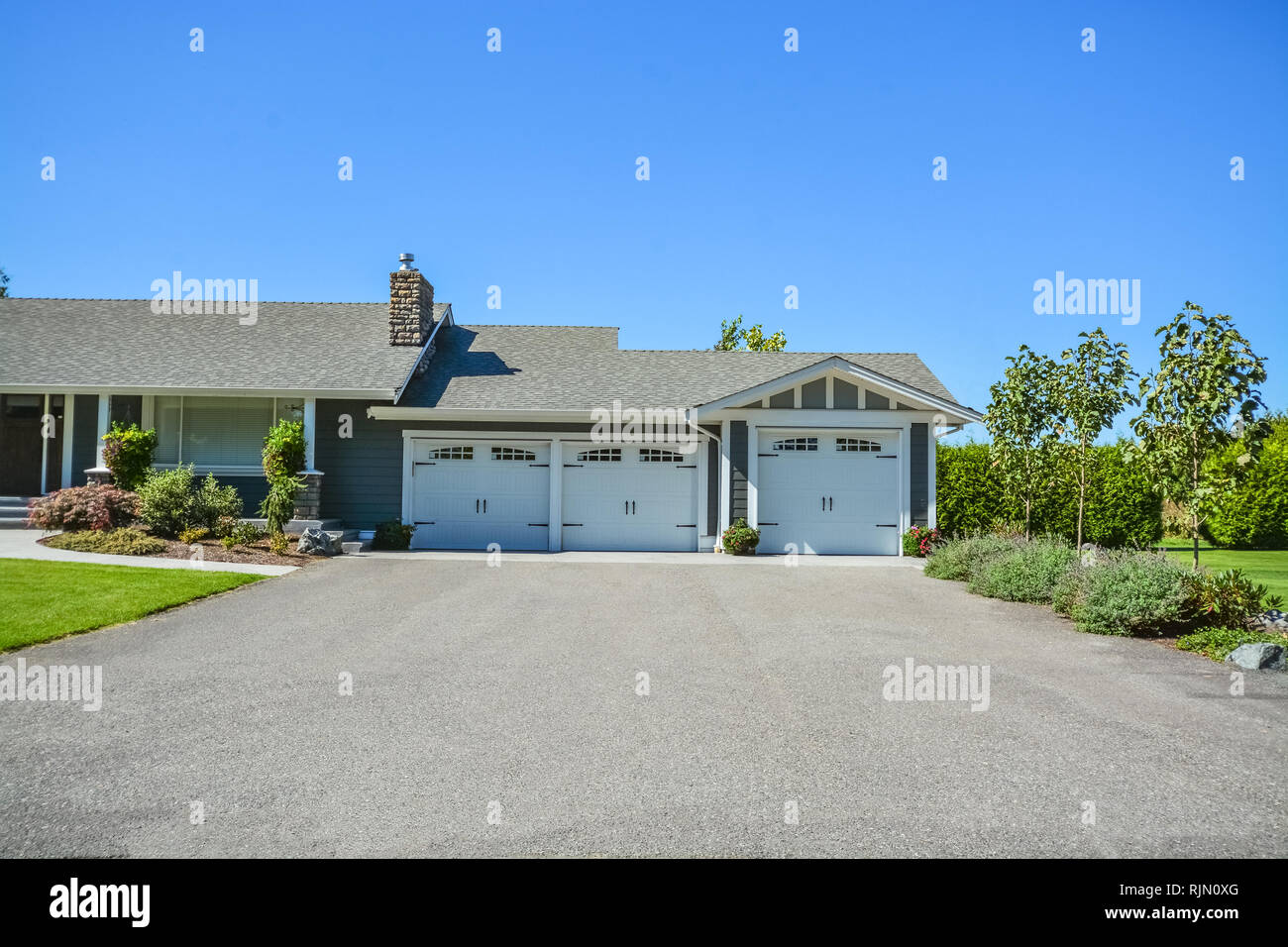 Wide asphalt driveway of residential house with three door garage ...