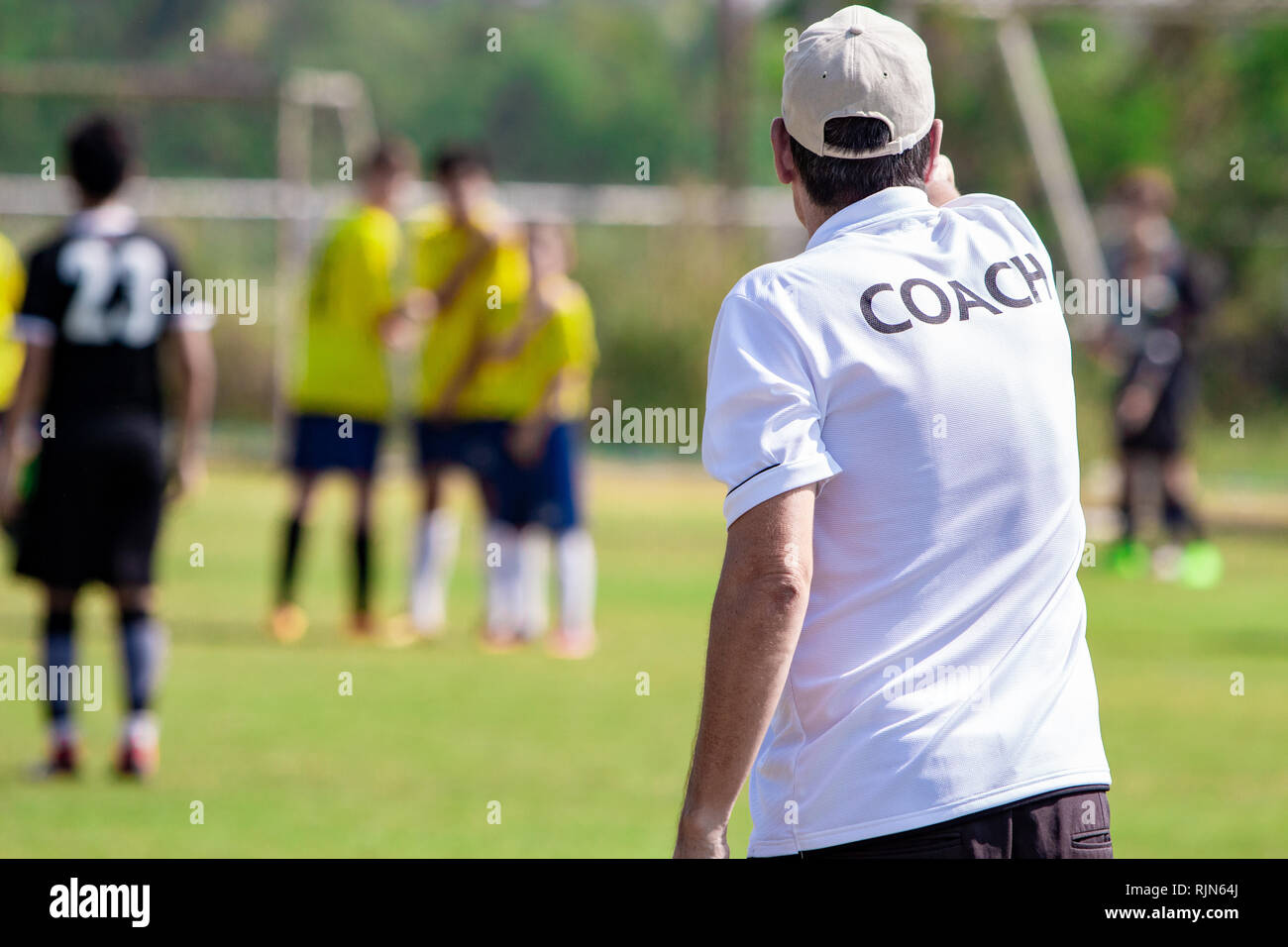 Back Of Football Coach Wearing White Coach Shirt At An Outdoor Sport Field Coaching His Team