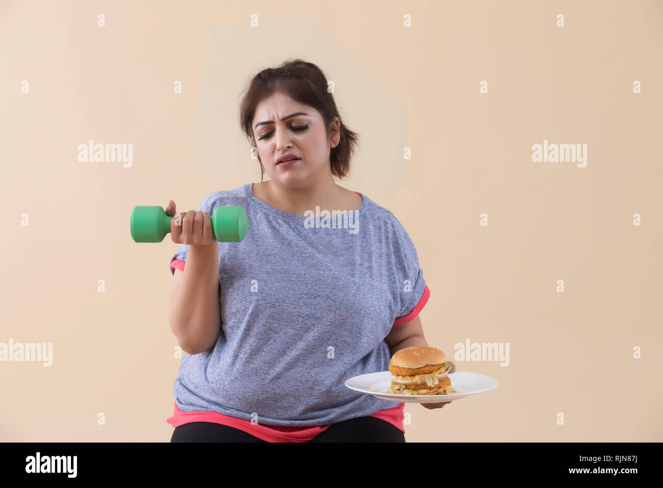 Sad Overweight Woman holding a burger and dumbbell Stock Photo - Alamy