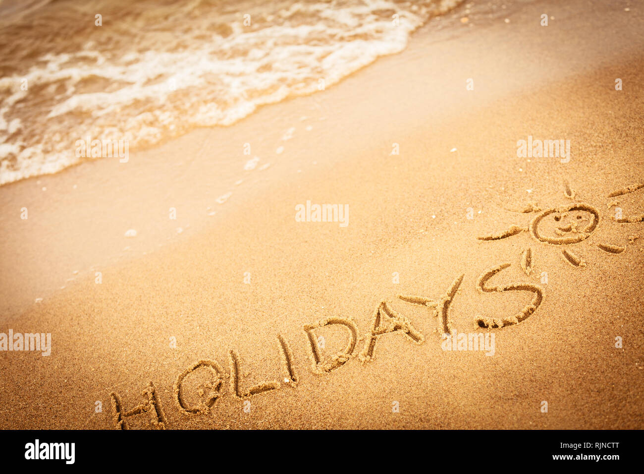 Summer vacation concept. The word holidays written in the sand on beach ...