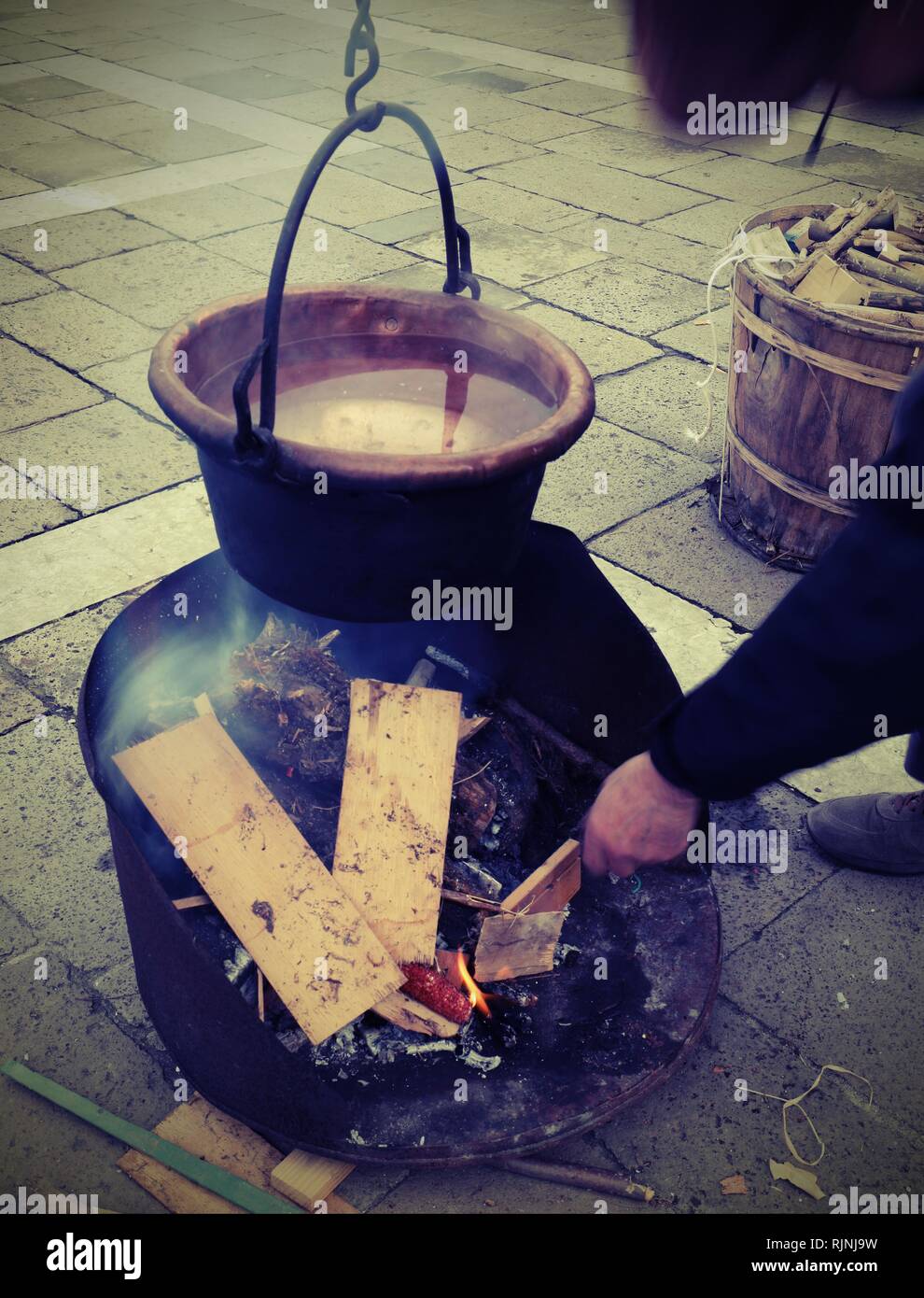 man feeds the fire lit to boil the water inside the old copper pot ...