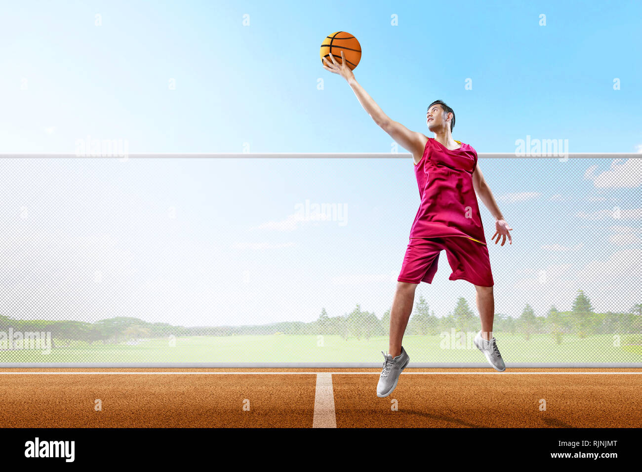 Excited asian basketball player man with ball in hand jumping high on ...