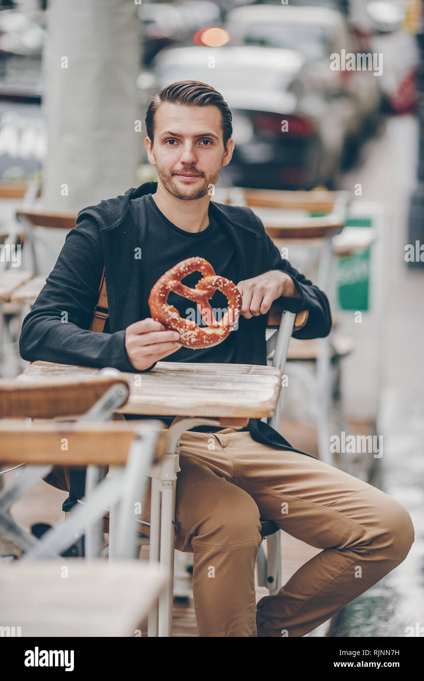 Happy young man eating pretzel outdoors in Europe Stock Photo - Alamy