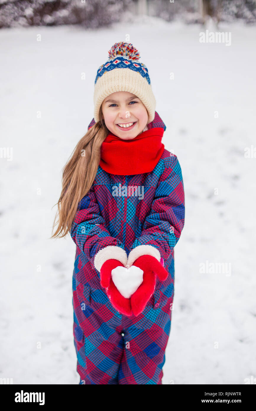 A girl in red gloves holds a heart shaped snowball. Symbol of love for ...