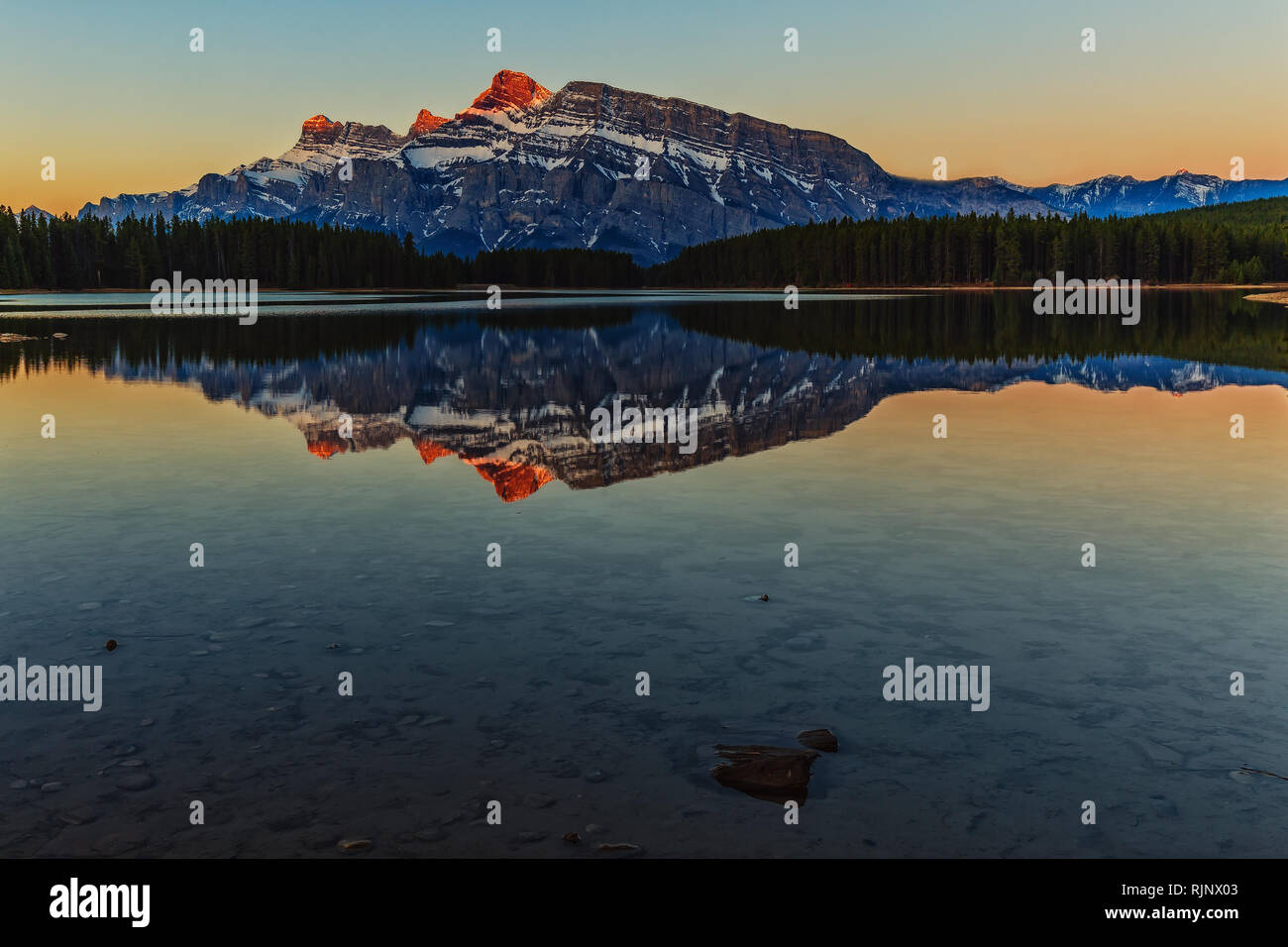 Snow-covered mountains are reflected in Two Jake Lake and create a ...