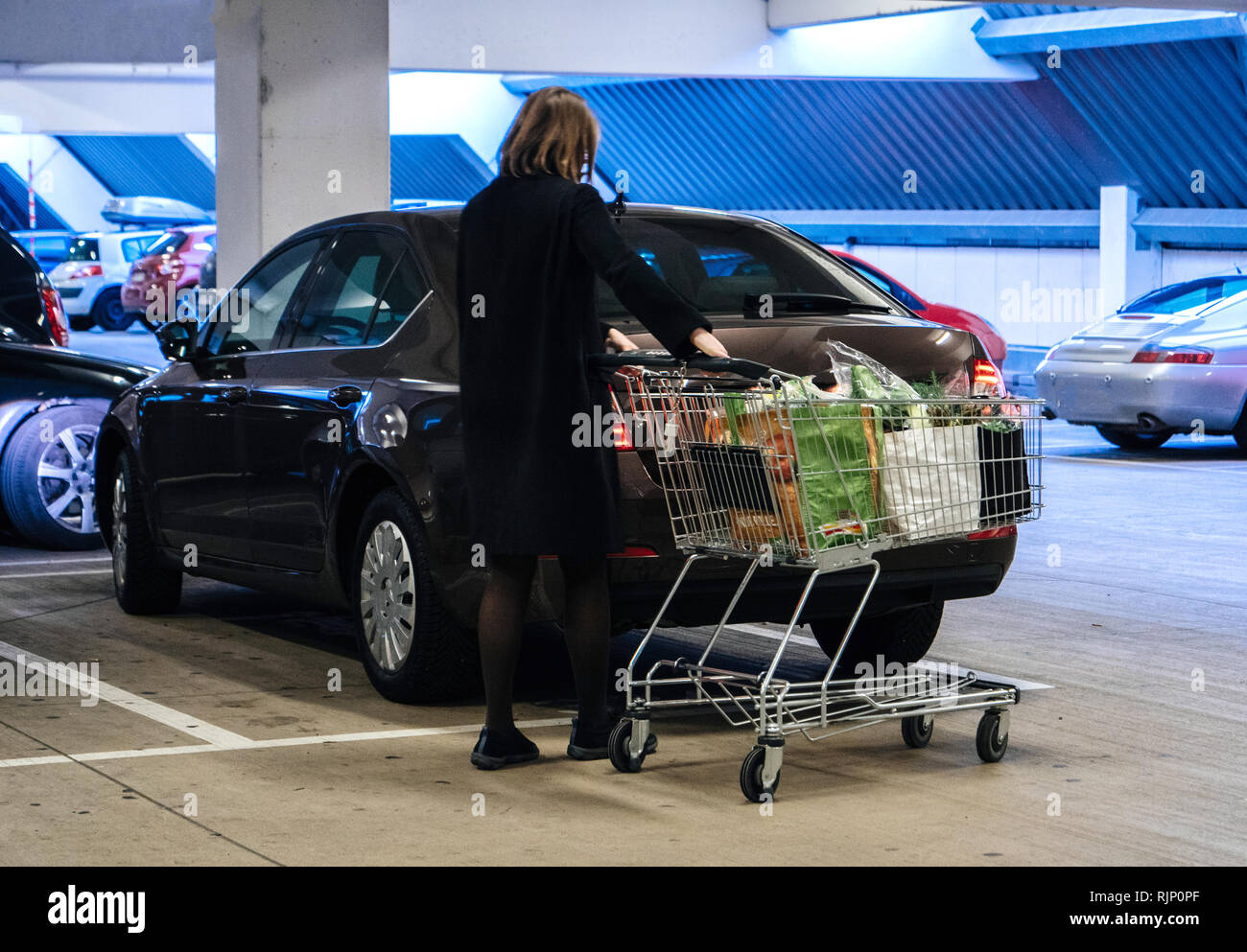 Side view of woman with shopping trolley near car putting bags with ...