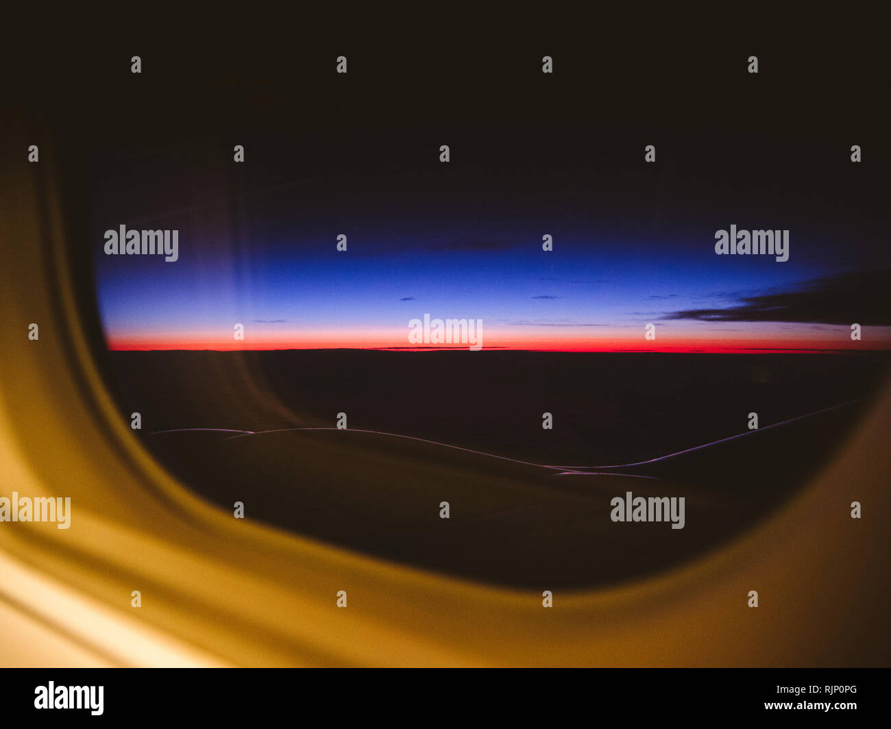 Shot through plane window of dusk time with dark clouds in sunset sky ...