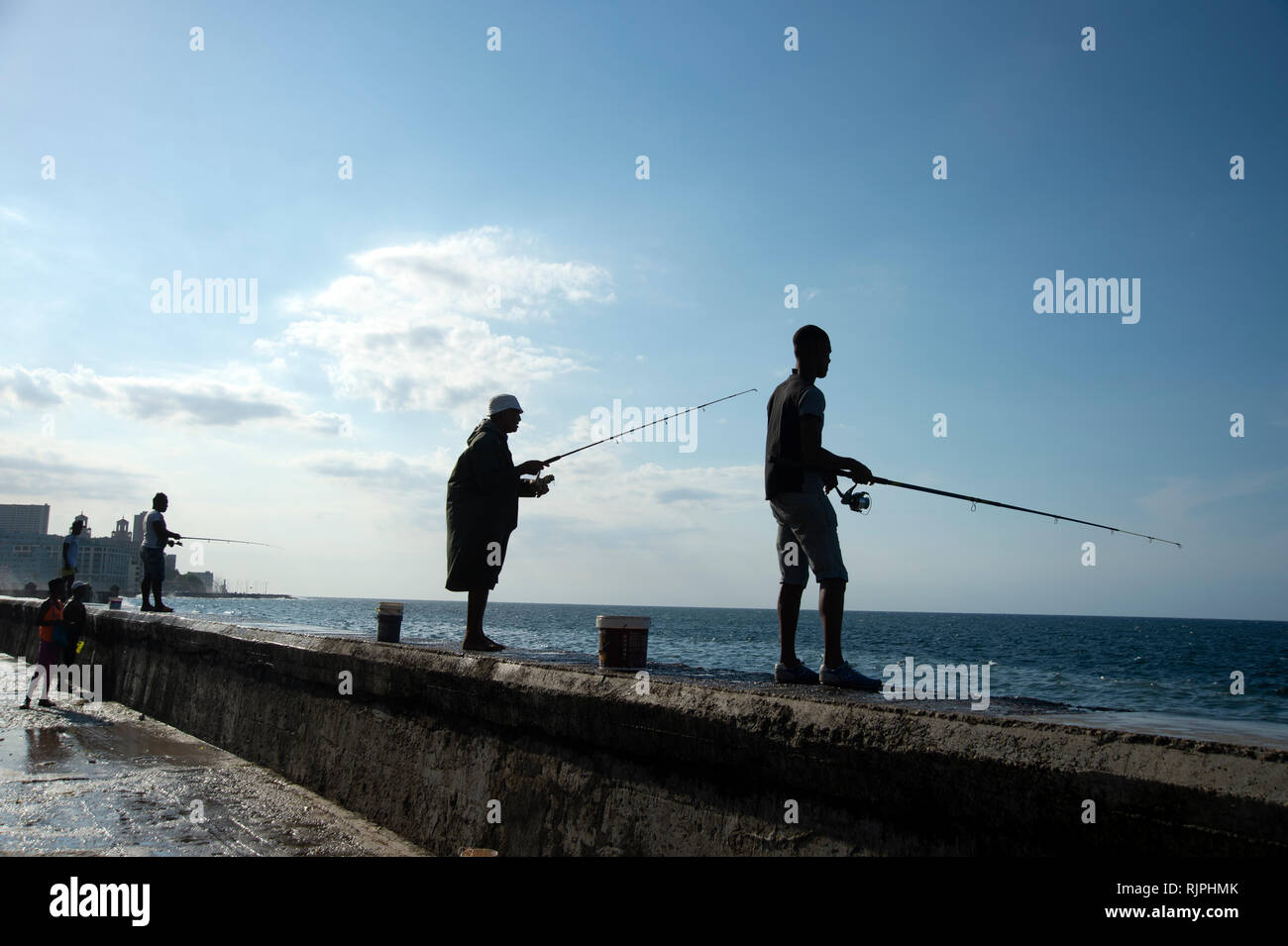 Three silhouetted Cuban fishermen fishing from the sea wall on the ...