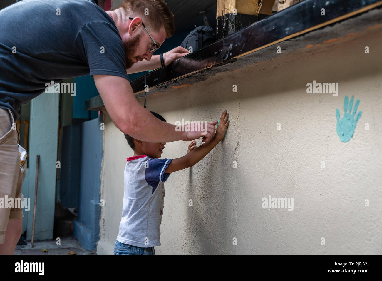 caucasian man helping lain boy make hand prints on wall in Guatemala ...