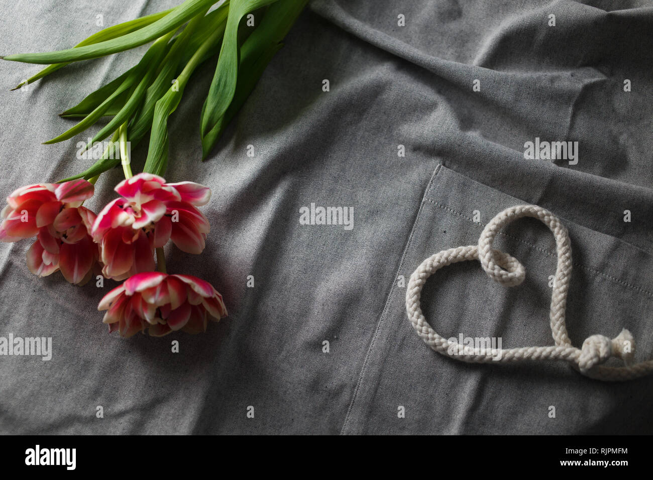 Heart from rope and bouquet of tulips on a gray background with space ...