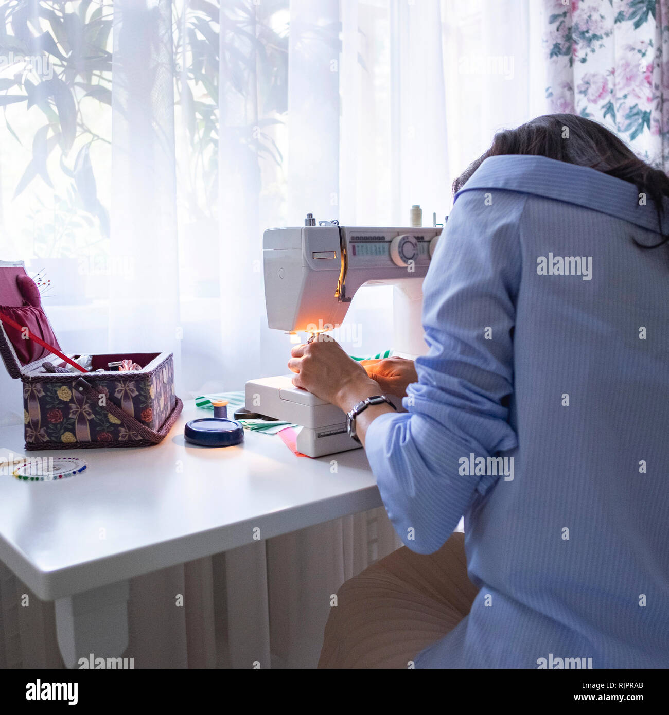 Woman threading sewing machine needle beside window Stock Photo - Alamy