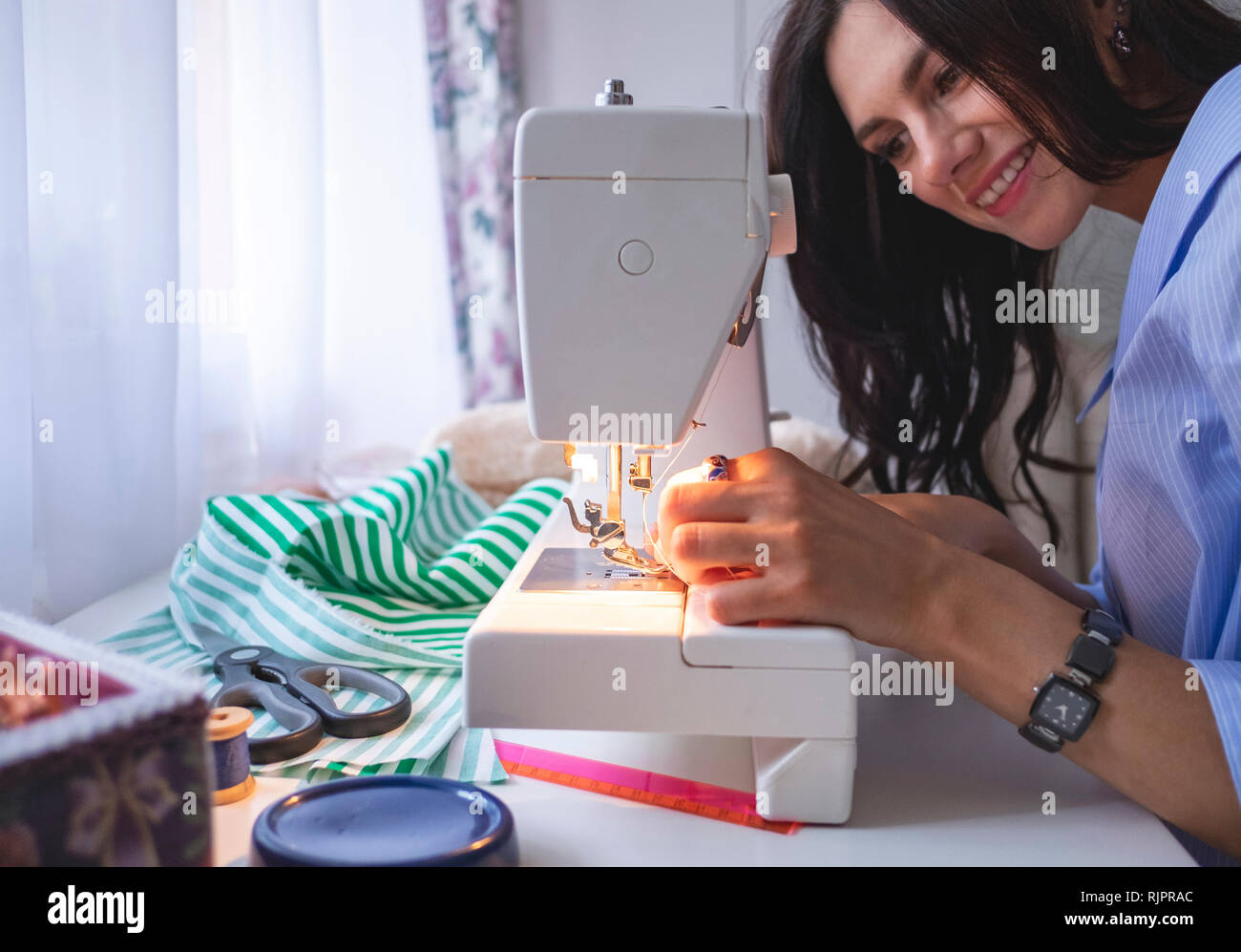 Woman threading sewing machine needle beside window Stock Photo - Alamy