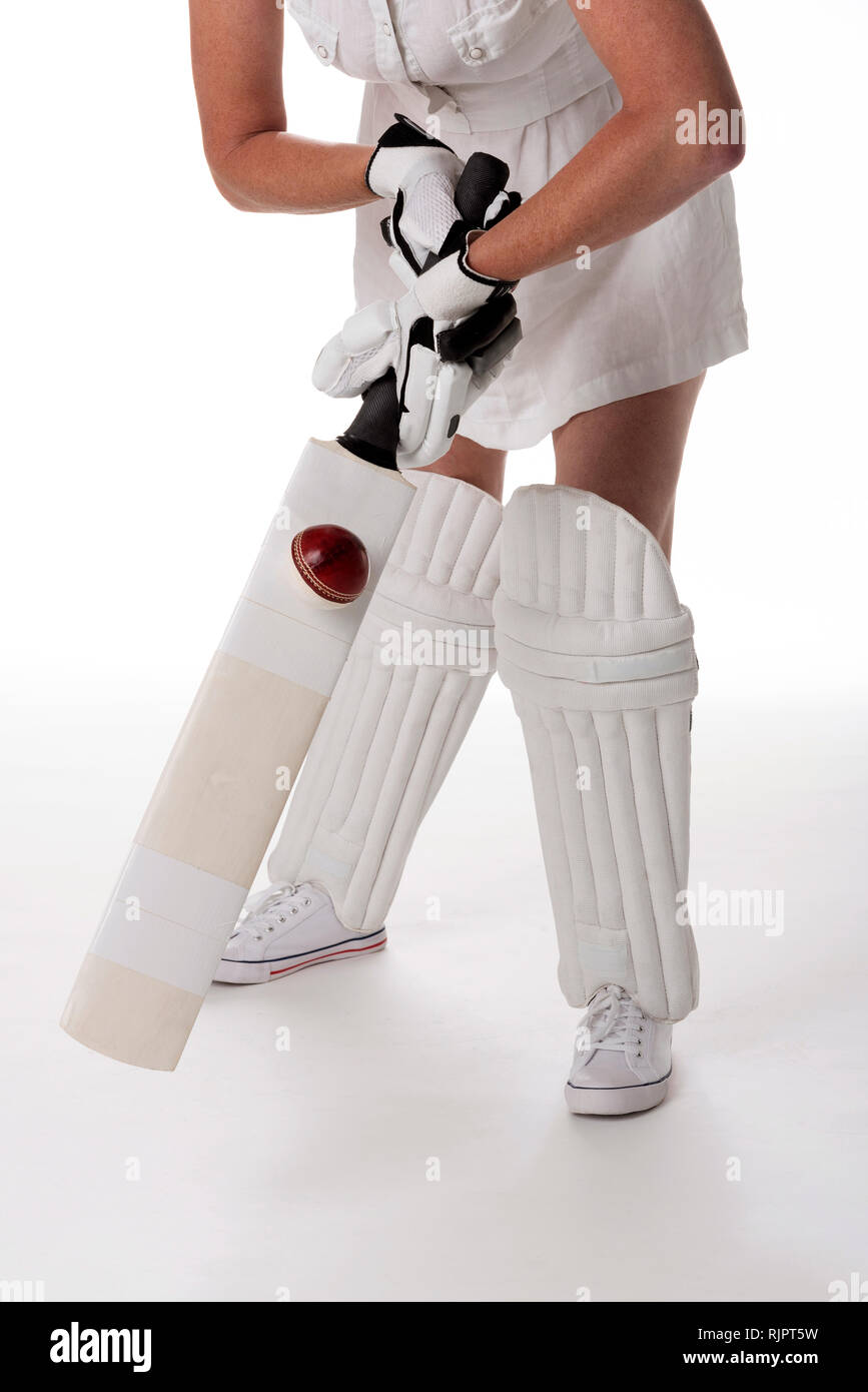 Woman cricketer in a white dress with a safety helmet, shin pads, a bat ...