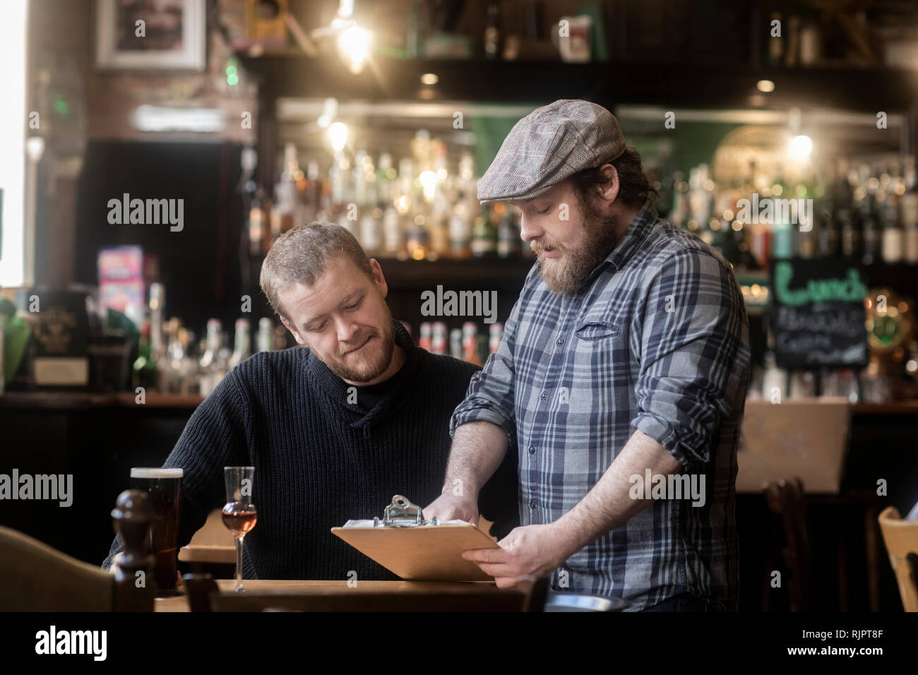 Barman looking at menu with customer in traditional Irish public house ...