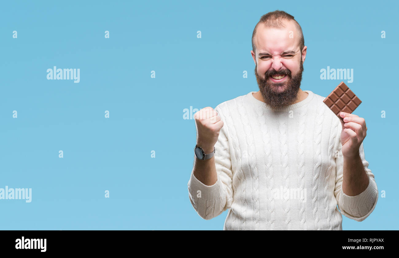 Young hipster man eating chocolate bar over isolated background ...