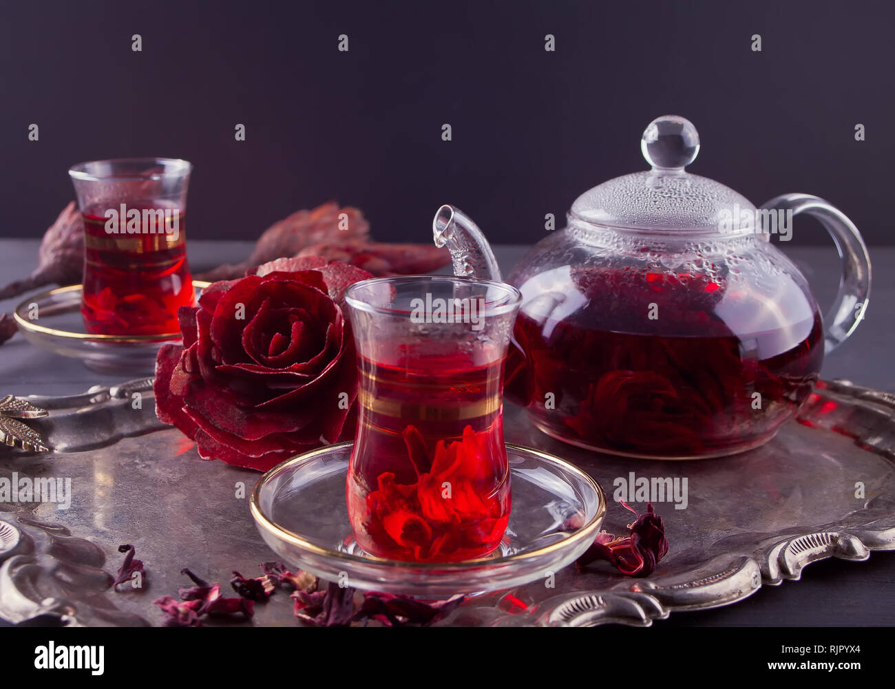 Cups of hot red karkade tea with teapot on the tray on the black table ...