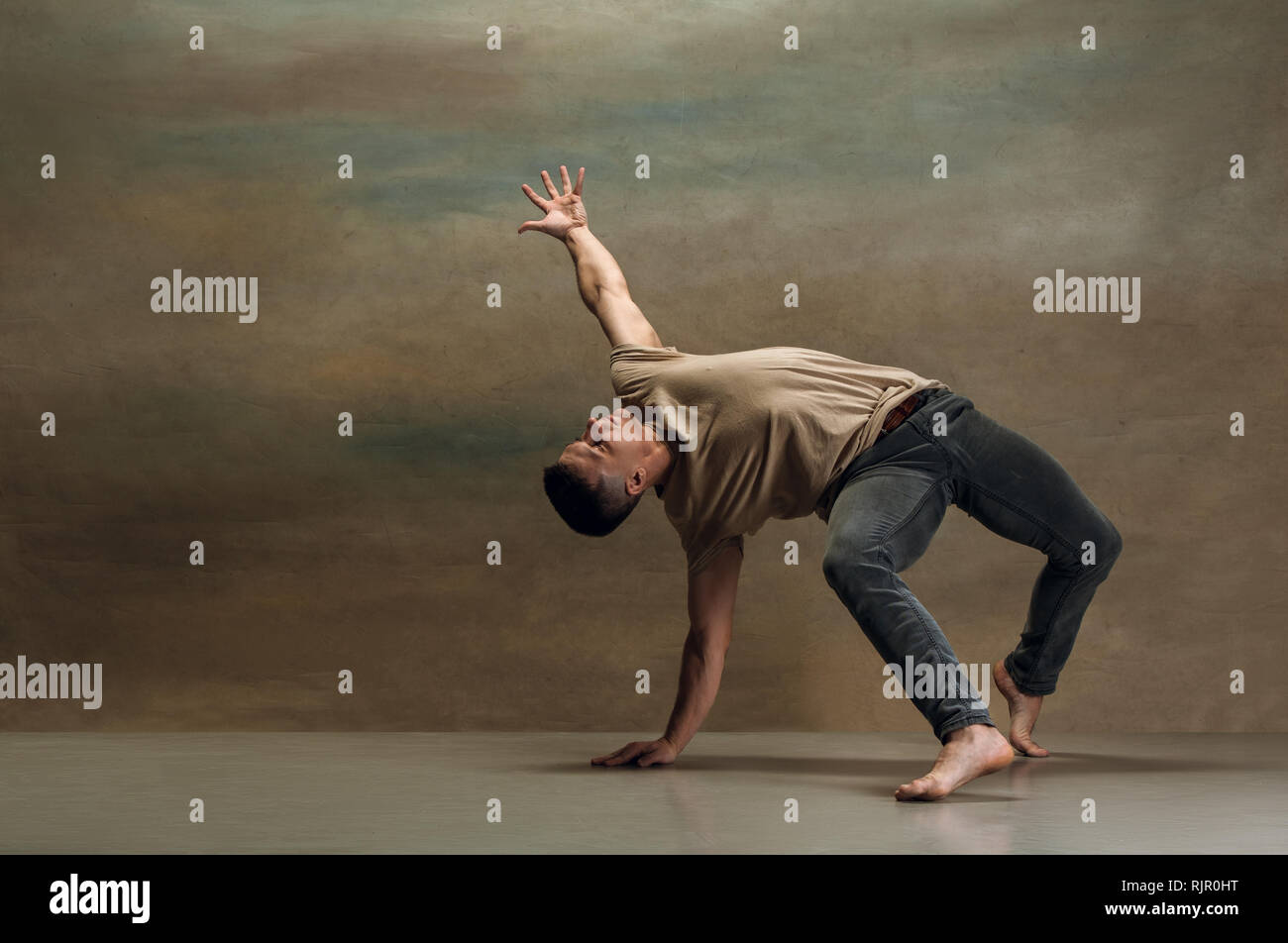 The young man dancing in contemporary stile of ballet at studio on gray ...