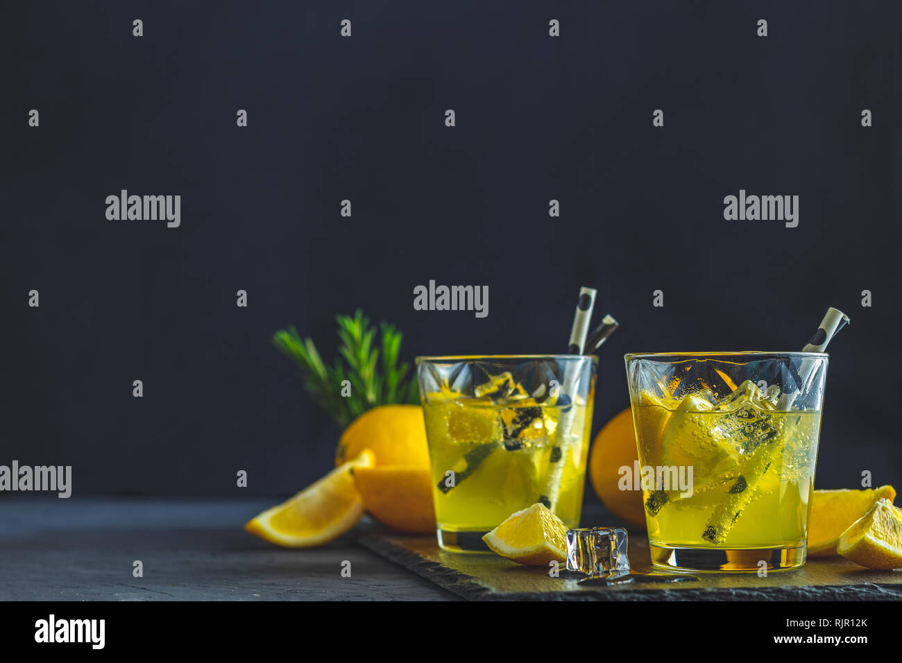 Lemon alcohol drink cocktail with ice, lemon and rosemary herb on black ...