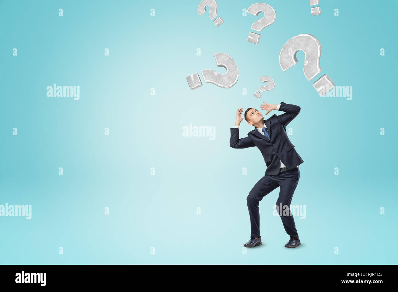 Grey question marks falling on a businessman on blue background ...
