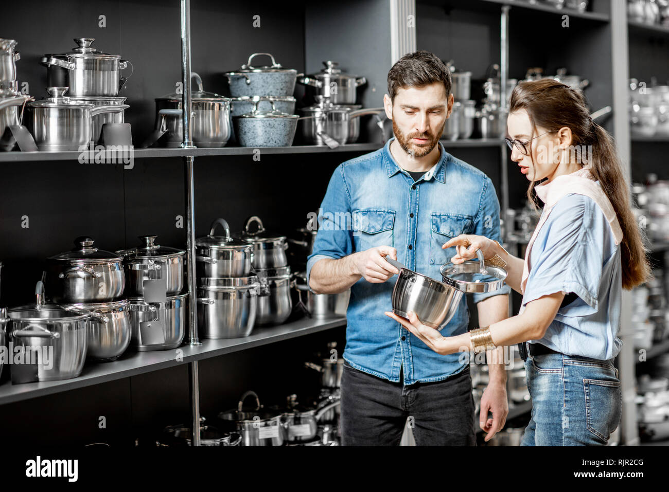 Young couple choosing pans for cooking in the department with kitchen ...