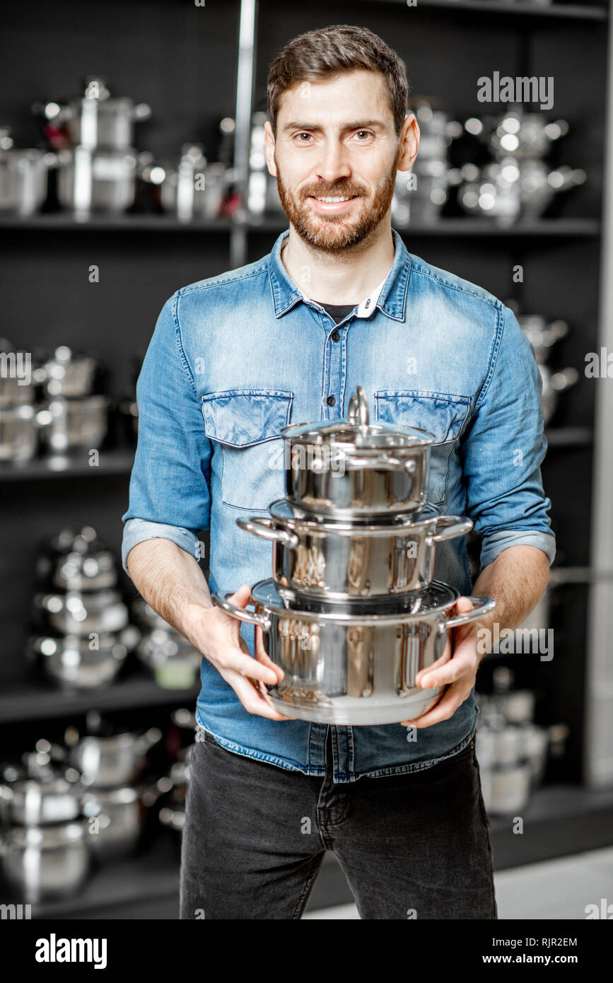 Handsome man holding pans for cooking choosing kitchen utensils in the ...