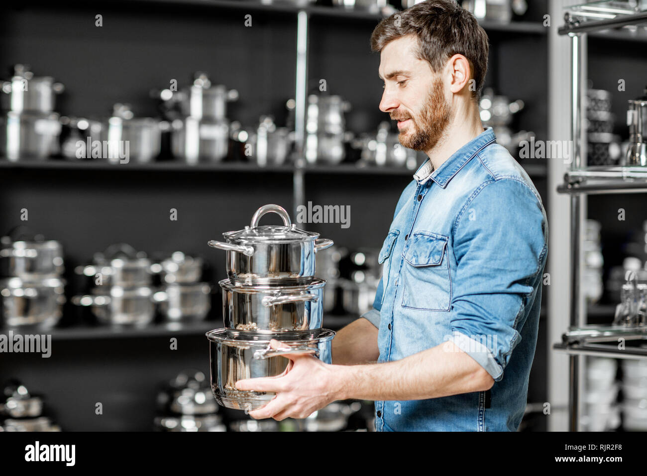 Handsome man holding pans for cooking choosing kitchen utensils in the ...